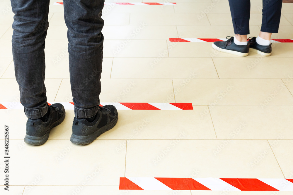 People stand in line keeping social distance, standing behind a warning ...