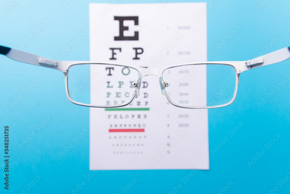Hand-held glasses, view of the Snellen chart. Eye examination. Blue ...