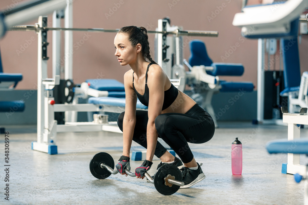 Young slim woman in a gym perfoms squats exercises with a barbell ...