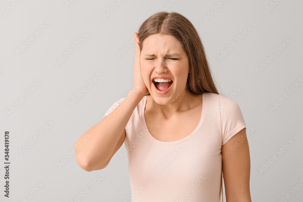Young woman suffering from loud noise on light background Stock Photo ...