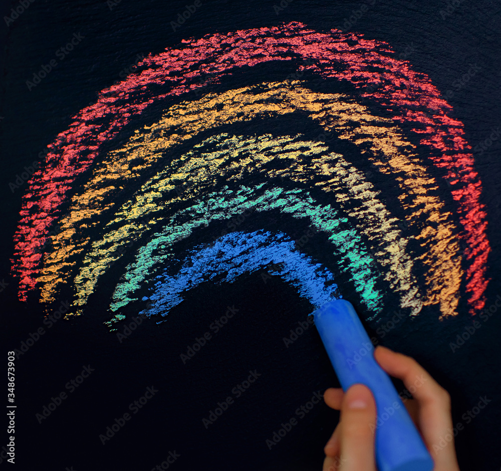Child's drawing of a rainbow with colorful chalk on a black rough ...