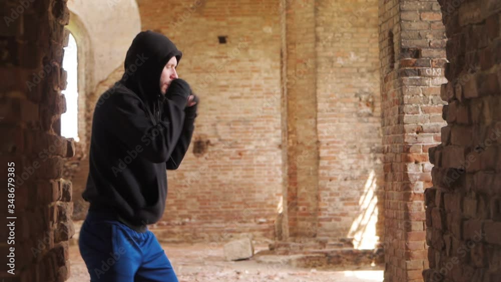 Man boxer in the hood trains beats in an abandoned building. Shadow ...