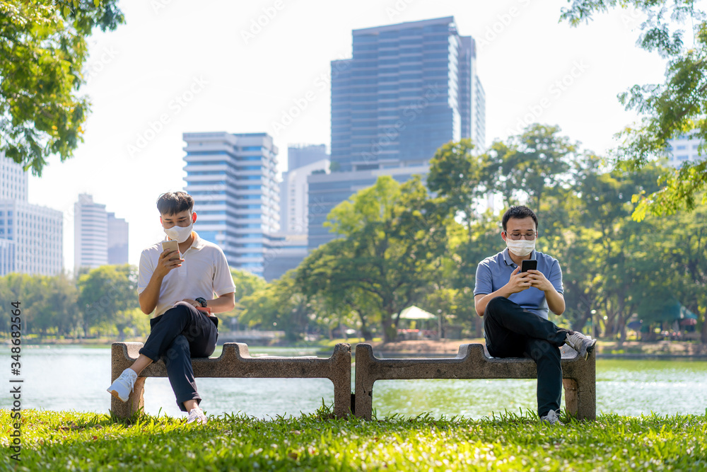 Two Asian young man chatting in smartphone and wearing mask sitting ...