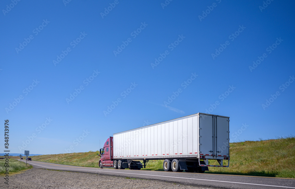 Dark red big rig semi truck transporting commercial cargo in dry van ...