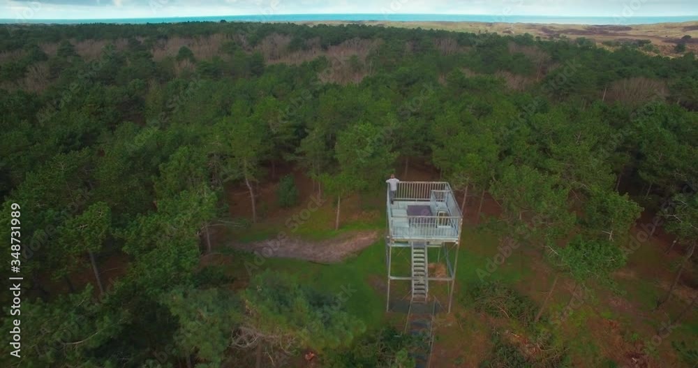 Young lonely boy or man standing on watchtower looking over the trees ...