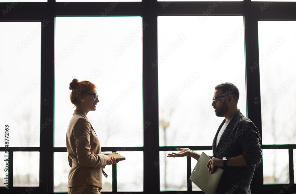 Two business partners talking to each other while standing in front of ...