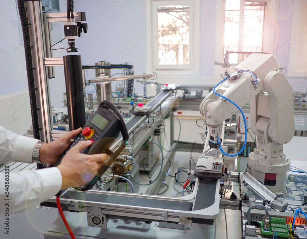 Close up of man's hand holding teach pendant to control robot arm which is integrated on smart ...