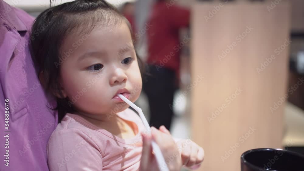 Asian girl toddler chewing plastic straw, baby enjoy eating and sitting ...