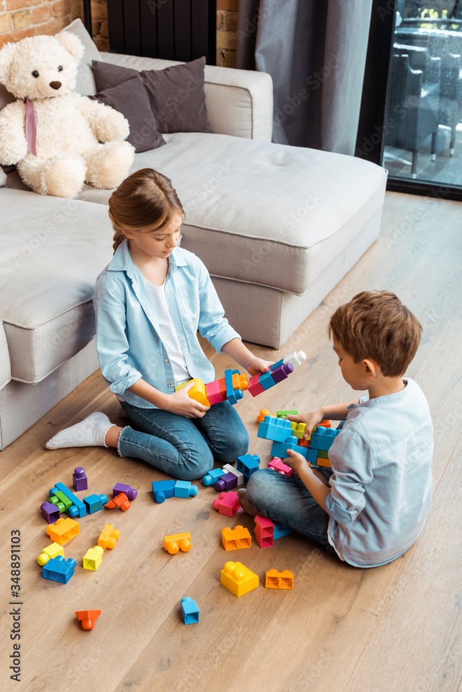 siblings playing with building blocks while sitting on floor in living ...