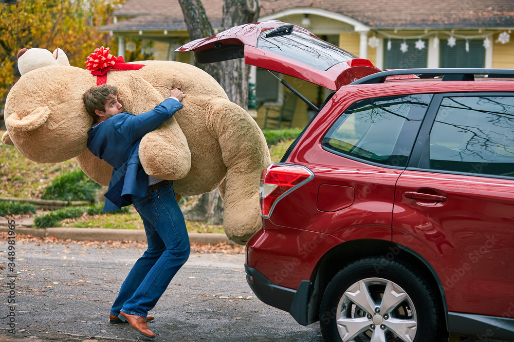 A goofy young man struggling to pull out an oversized teddy bear ...