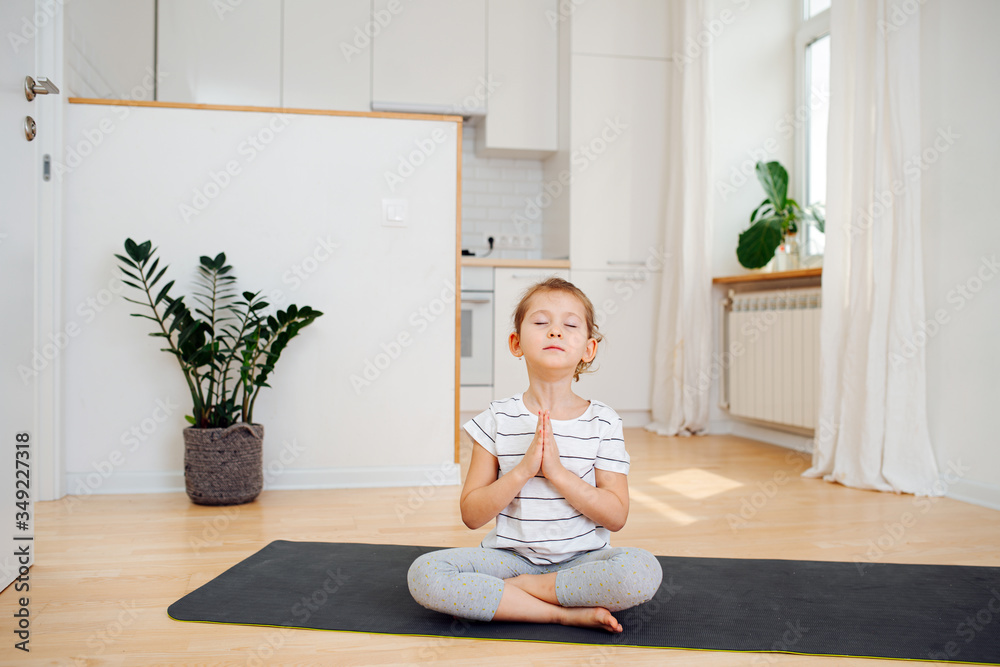 Preschooler girl sitting in easy pose with joined hands in a kitchen at ...