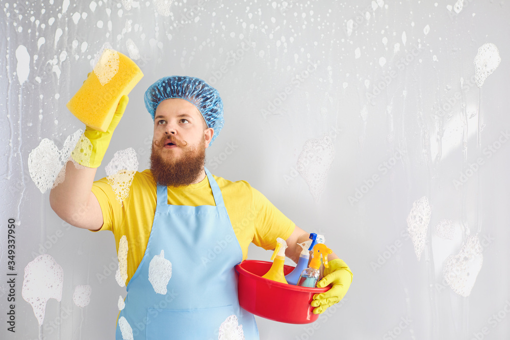 Funny fat man with a beard in an apron washing cleans up on a gray ...