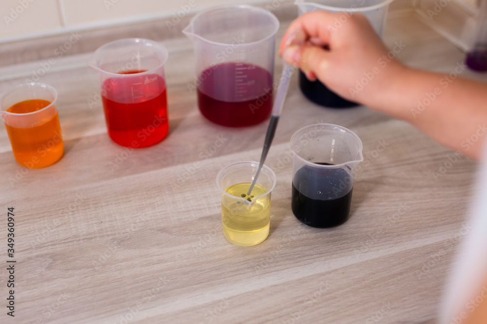 Girl adding drops of colored water to an oil glass. Density and ...