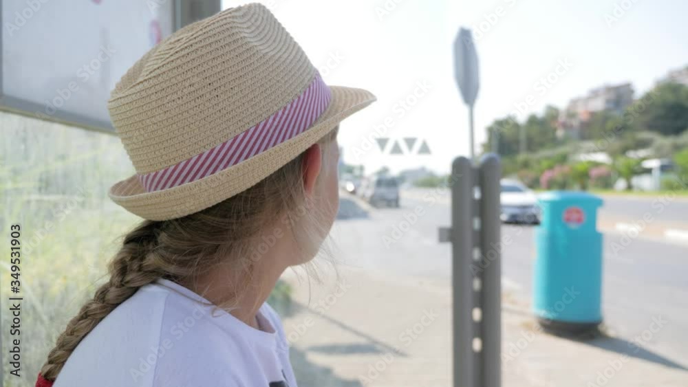 Little girl sitting on a bench waiting for transport at the bus stop ...