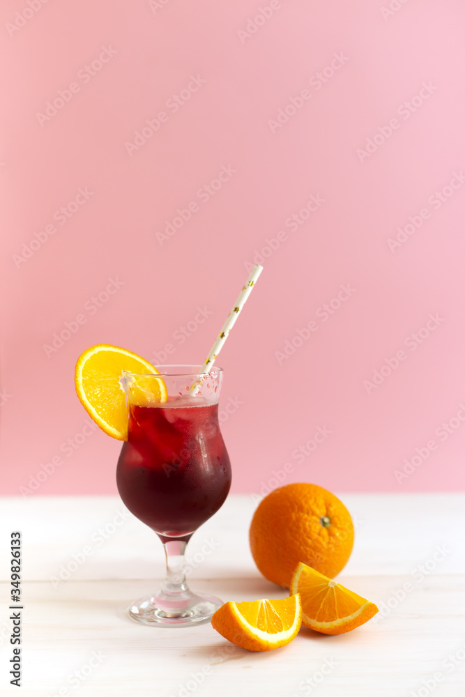 Hibiscus flower juice in glass with ice and oranges on pink and white ...