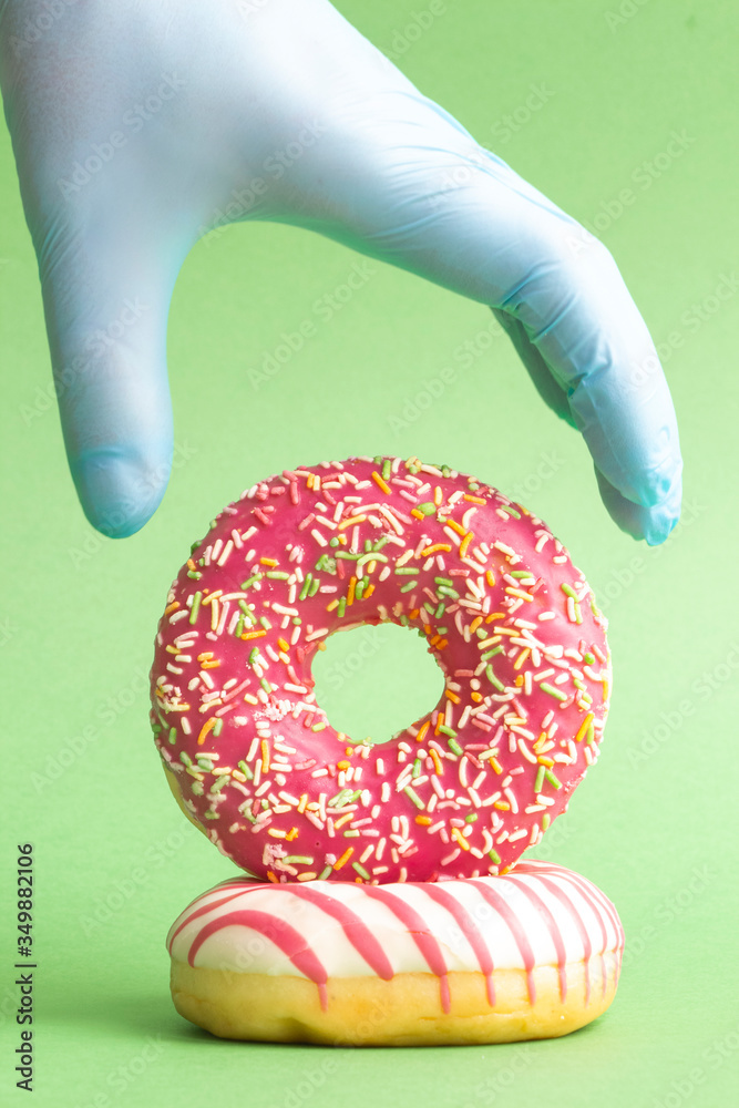 Person in blue surgical gloves reaches for donuts on a green background ...