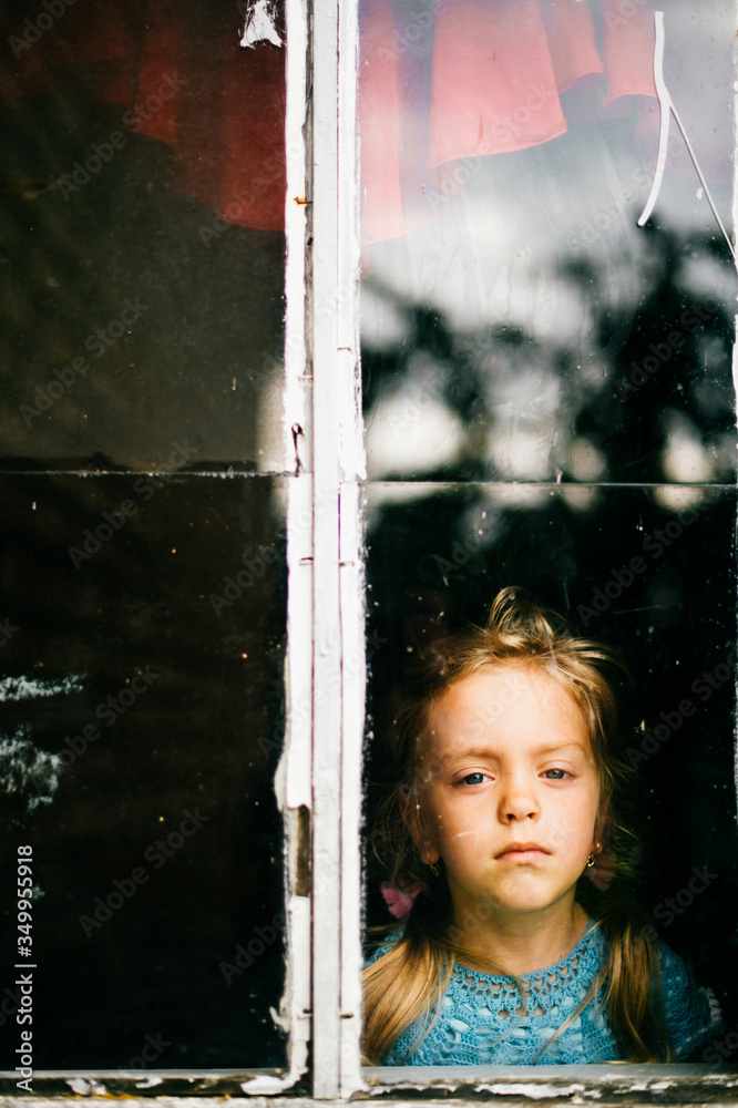 Lonely abandoned unhappy little girl looking through window with ...