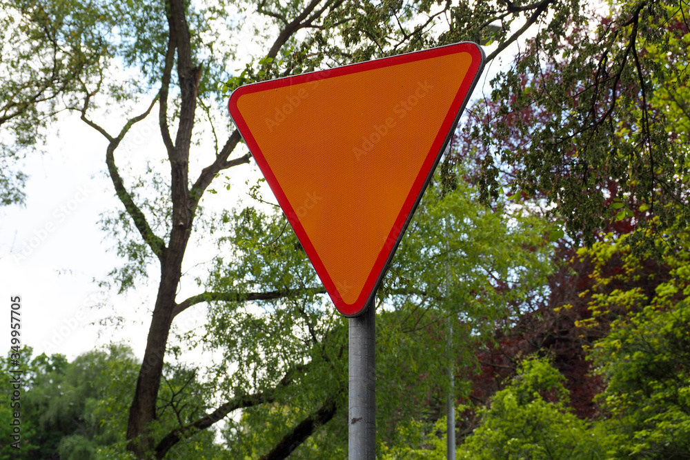 road sign give way on the background of trees and sky. a metal inverted ...