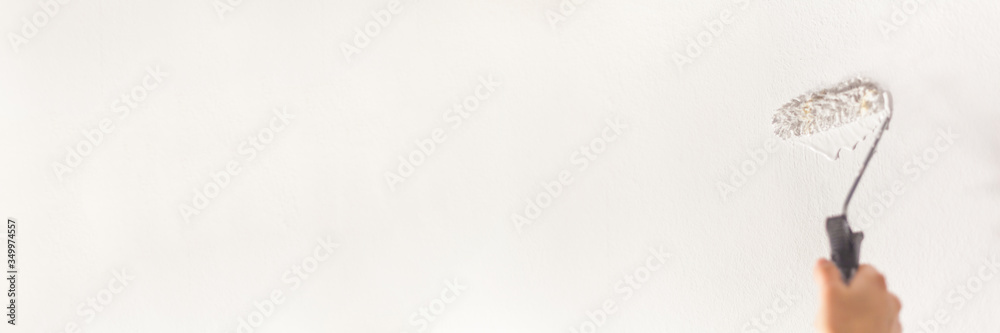 Human hand with small paint roller begins to paint a white wall craft ...