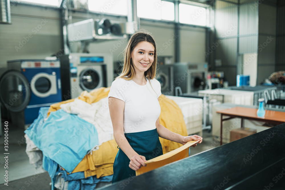 Young laundry worker pats the linen on the automatic machine at the dry ...