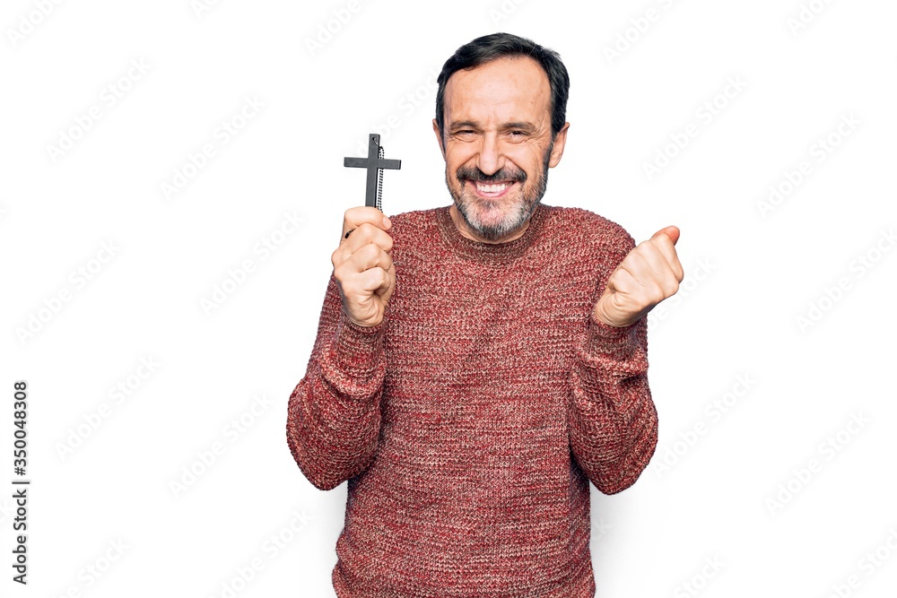 Middle age handsome catholic man praying holding christian cross over ...