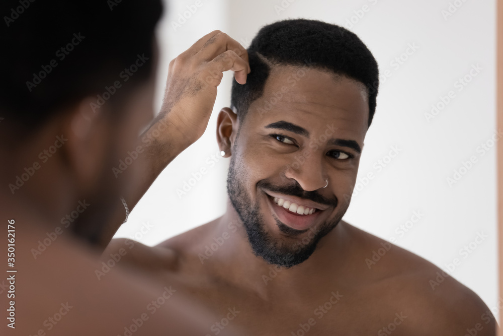 Smiling african American young man look in mirror in bathroom get ready ...
