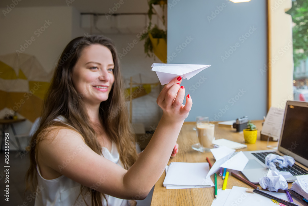 Focussed paper airplane in female hand. Blurred woman woman launches ...