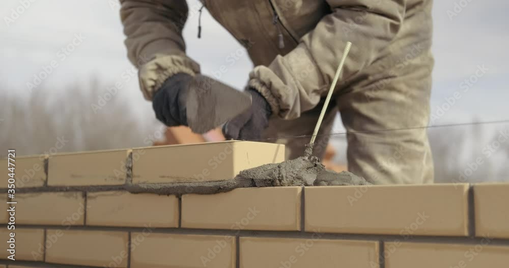 Bricklayer works at construction site, lays bricks in masonry, builds ...