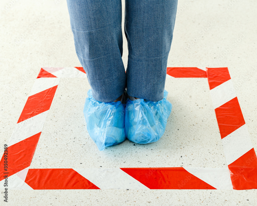Woman stand in line keeping social distance wearing overshoes, medical ...