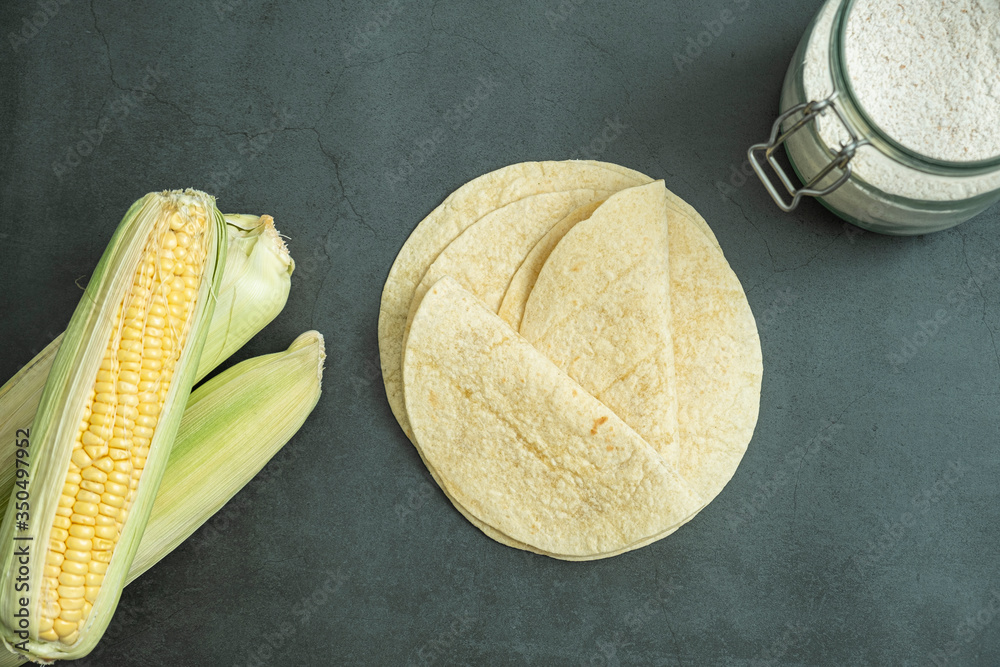 Fresh baked tortilla bread, corn flour in jar and green corn cobs on ...
