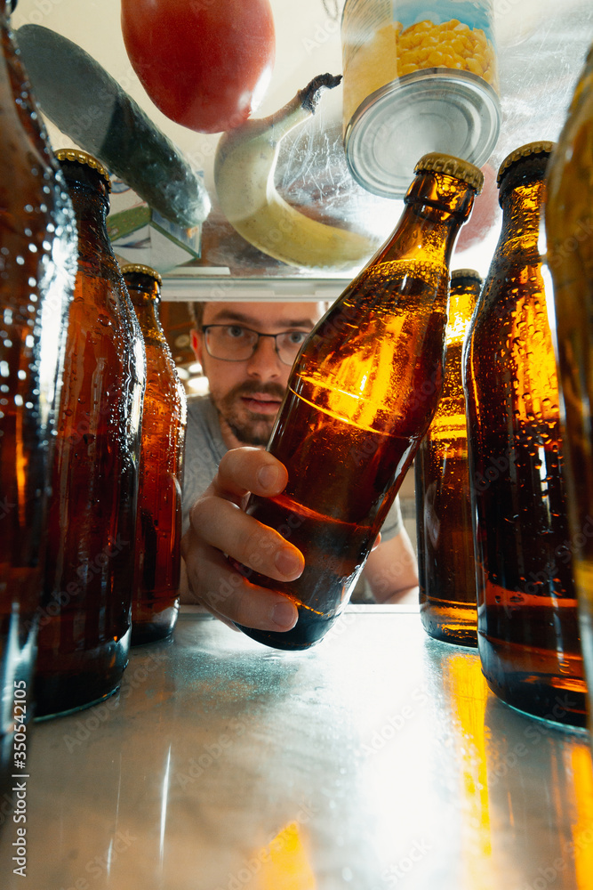 Caucasian man takes cold refreshing beer from out the fridge, inside ...