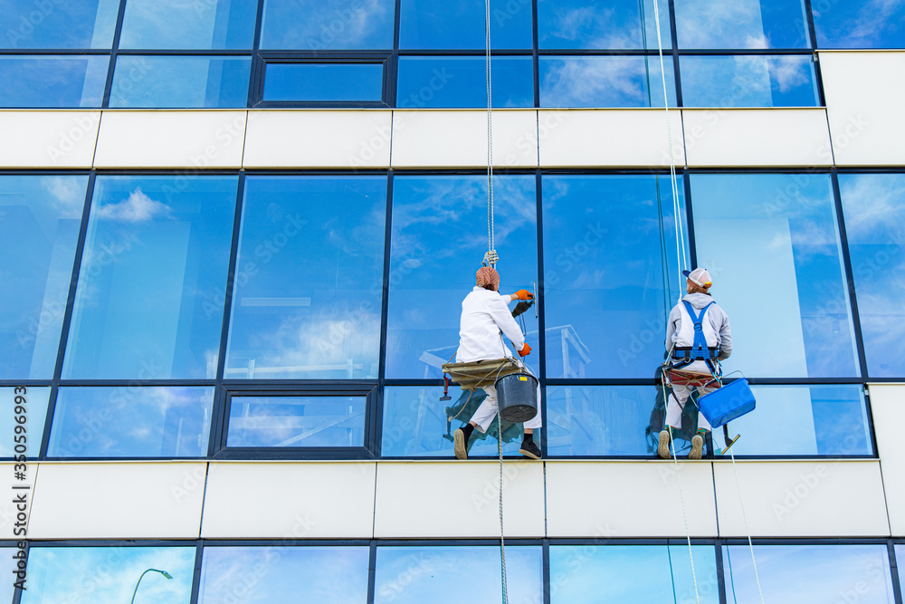 window cleaner workers back to camera on high outside of modern office ...