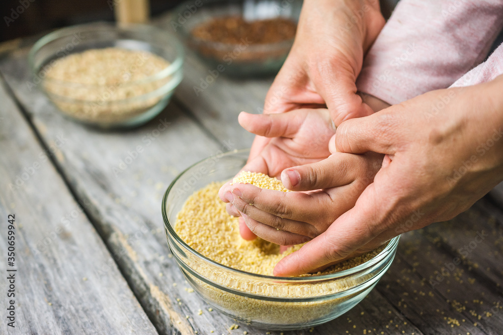 Mother and child's hands grabbing millet seeds from the glass bowl ...