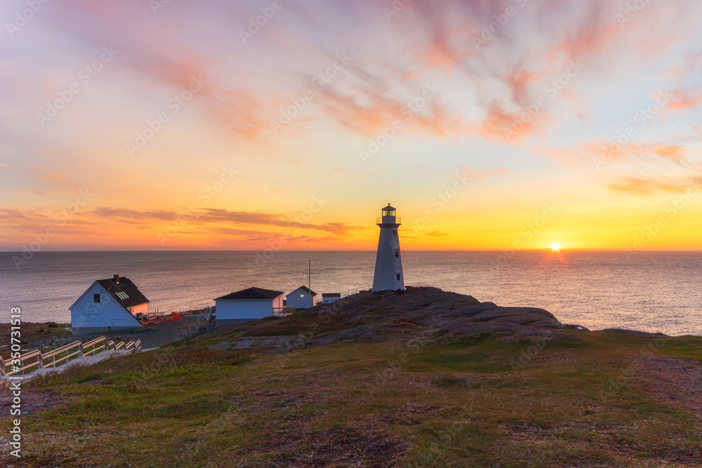 Foto de Beautiful sunrise over a white lighthouse sitting at the edge ...