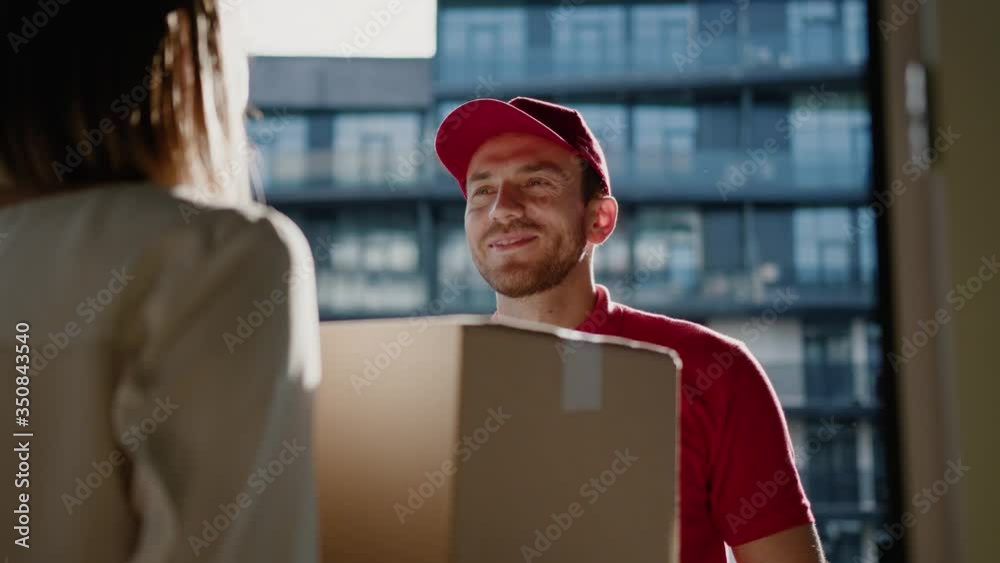 Stockvideon Cheerful handsome postman in red uniform delivering big ...