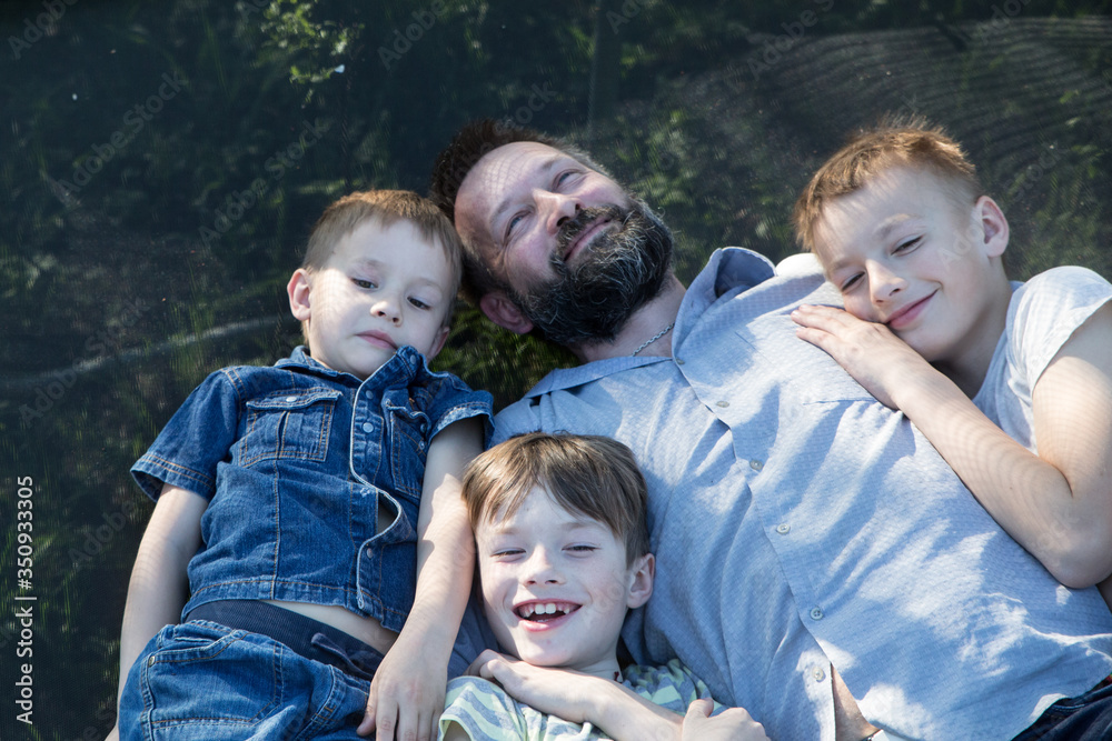 happy dad and his three sons lie on a trampoline and hug Stock Photo ...