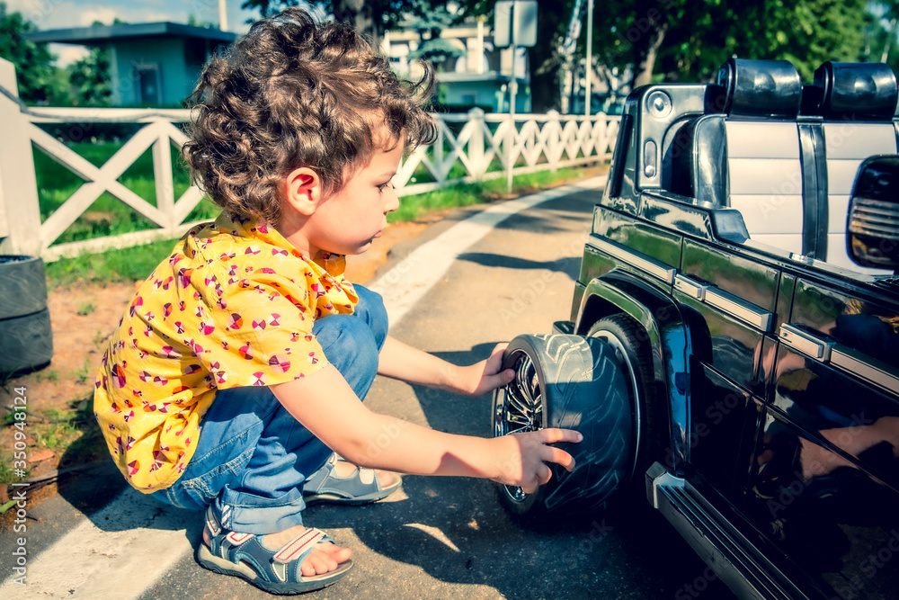 Foto de Young boy changing a tire on an black toy car. Children in the ...