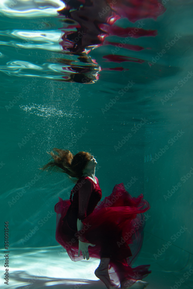 Beautiful girl underwater in a red dress swims in the pool. Tenderness ...