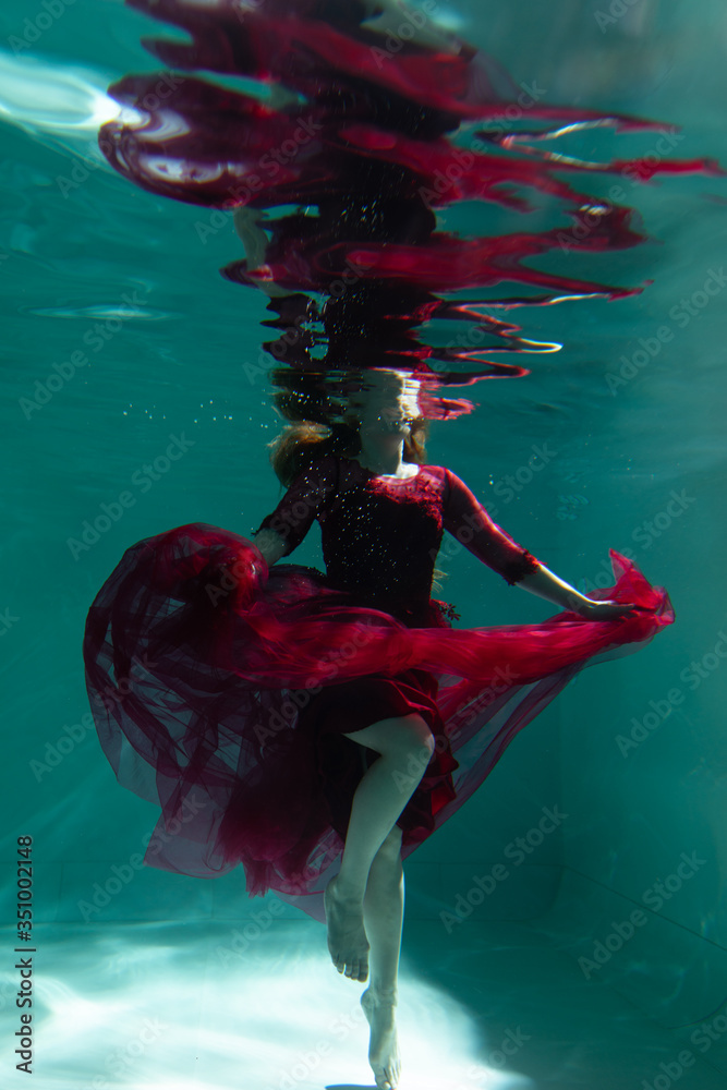 Beautiful girl underwater in a red dress swims in the pool. Tenderness ...