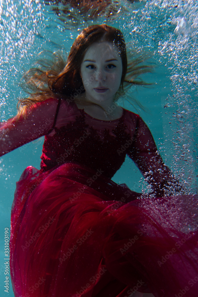 Beautiful girl underwater in a red dress swims in the pool. Tenderness ...