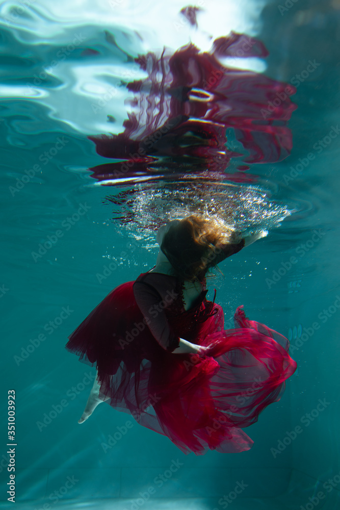 Beautiful girl underwater in a red dress swims in the pool. Tenderness ...