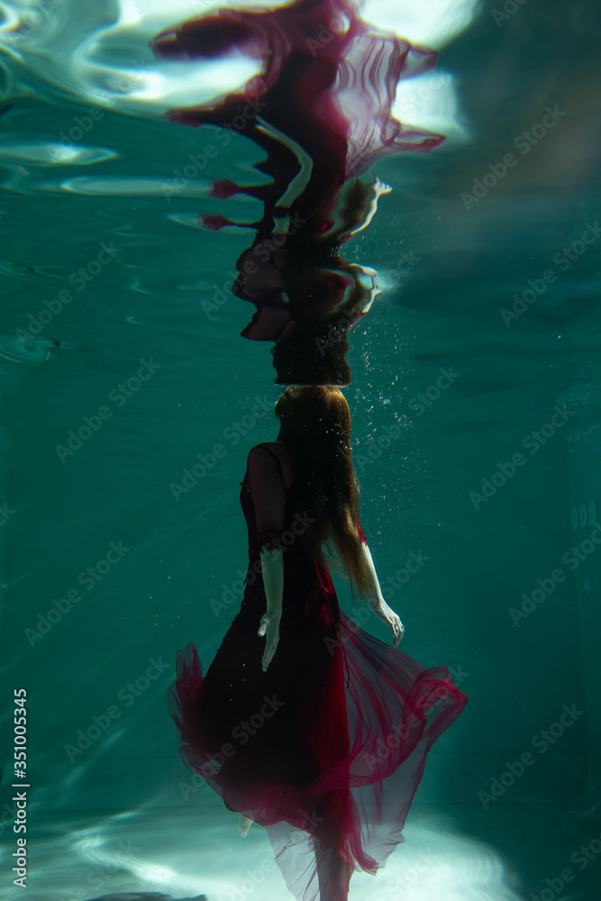 Foto de Beautiful girl underwater in a red dress swims in the pool ...