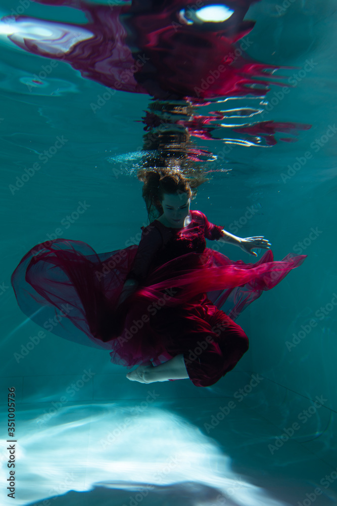 Beautiful girl underwater in a red dress swims in the pool. Tenderness ...
