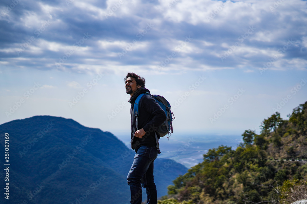 Young handsome indian boy standing on the top of the mountain with a ...