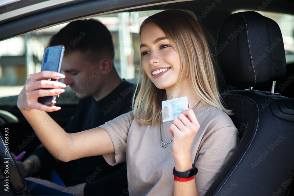 Happy smiling girl takes a selfie with a new drivers license, sitting ...