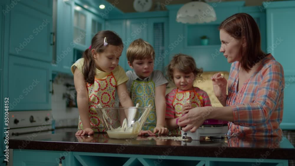 Young 30s mother with three kids in aprons making waffles in waffle ...
