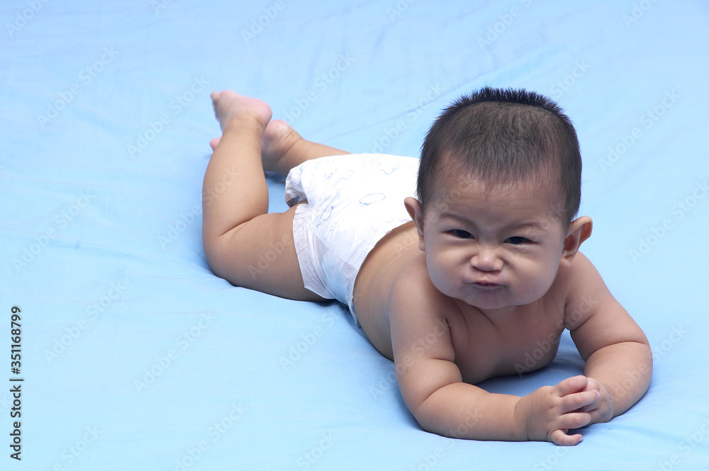 Baby in diaper lying forward on the bed making funny facial expression ...