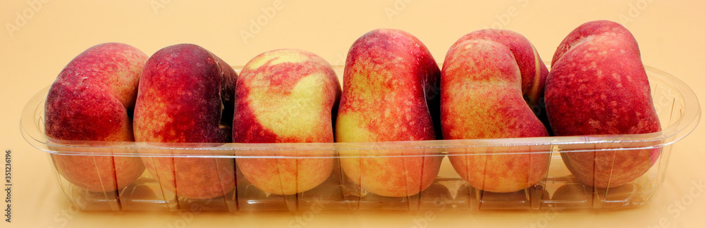 panoramic closeup of plastic punnet of ripe fresh fruit flat peaches in ...
