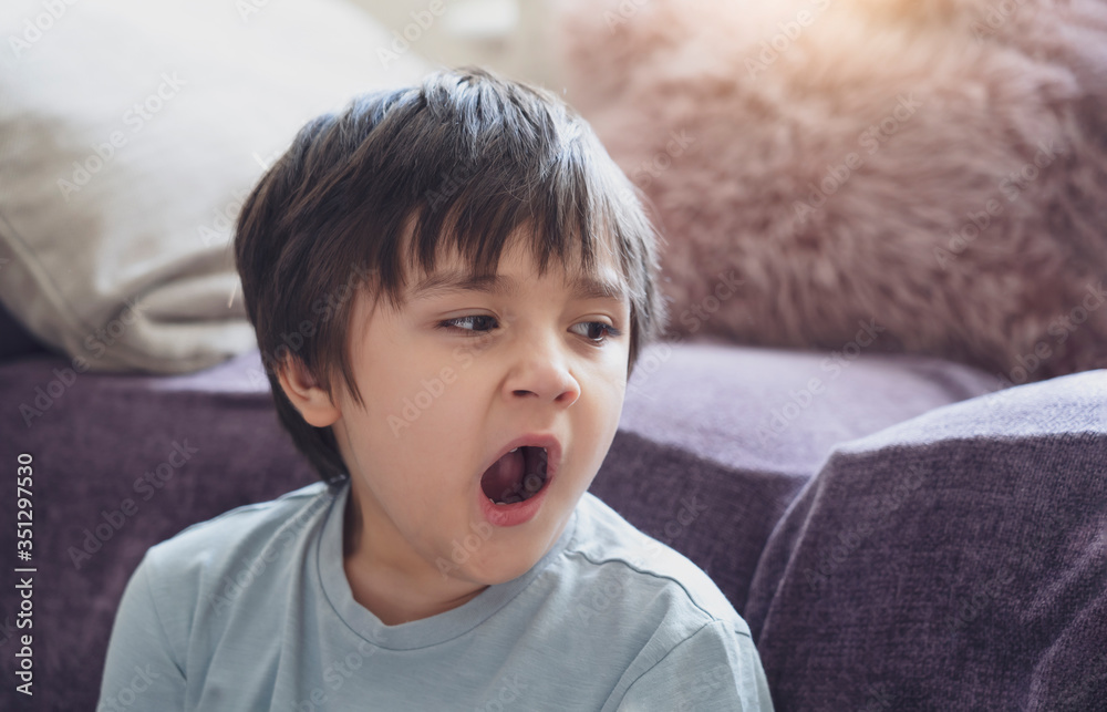 Portrait tired kid yawning sitting next to sofa, sleepy boy yawning and ...