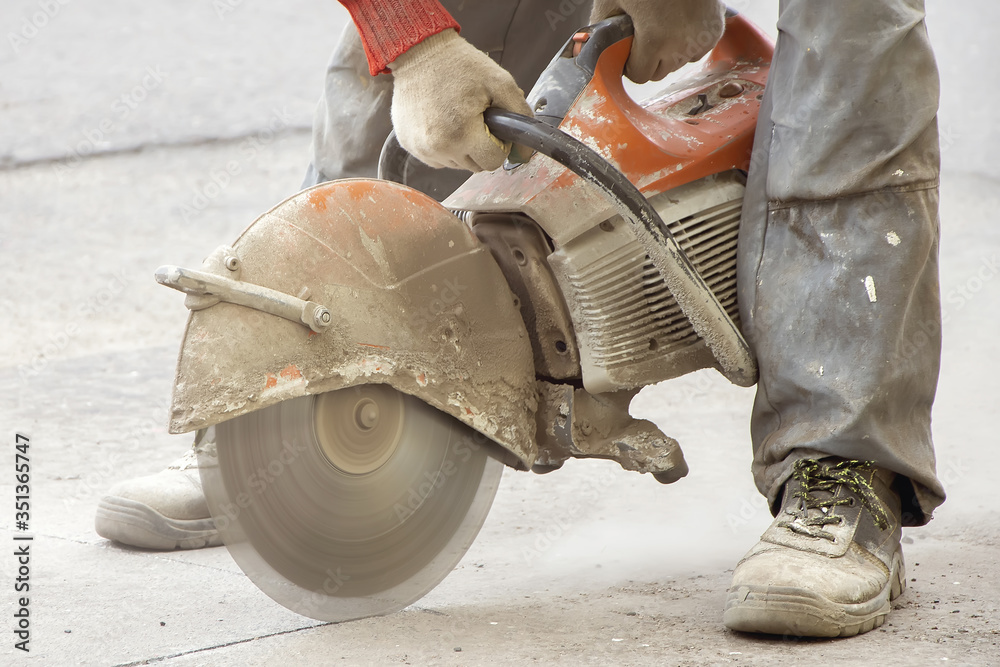 A male construction worker saws asphalt with a seam cutter, dust swirls ...